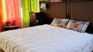Uma cama grande com um edredom branco, uma mesa de cabeceira com abajur e uma cortina verde.