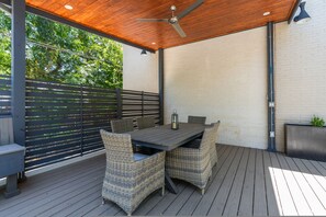 Um pátio ao ar livre com deck de madeira, uma mesa com cadeiras, um ventilador de teto e um candeeiro.