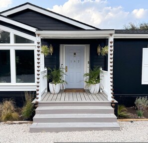 Uma casa com varanda frontal, uma porta branca e dois vasos de plantas em cada lado.