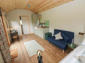 Um quarto com teto de madeira, um sofá, uma pequena mesa, um armário verde e uma porta que dá para outro cômodo.