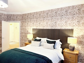Quarto com cama, duas mesas de cabeceira, cabeceira de madeira e uma porta.