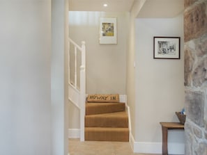 Uma escadaria com um travesseiro 'HOWAY IN', um quadro na parede e uma parede de pedra à direita.