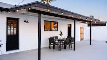 Alpendre coberto com mesa, cadeiras, planta em vaso e janela com vista.