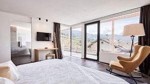 Quarto de hotel moderno com uma cama grande, uma escrivaninha, televisão e vista para o campo.
