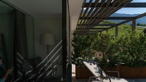 Quarto moderno com parede de vidro, sofá, mesa com uma garrafa de vinho e pérgola com vista para um vinhedo.