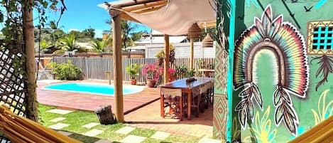 Uma rede, uma piscina, uma mesa com cadeiras e um mural.