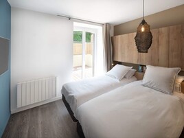 Quarto com duas camas, cabeceira de madeira, luminária pendente e vista para o exterior.