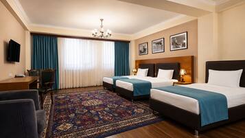 Quarto de hotel com duas camas, uma escrivaninha, uma cadeira, televisão e um lustre.