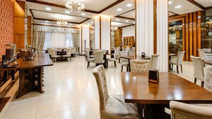 Uma ampla área de refeições com várias mesas e cadeiras, um lustre e uma parede de tijolos decorativa.