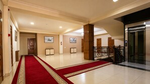 Um hall amplo com carpete vermelho, portas de madeira e um elevador moderno.