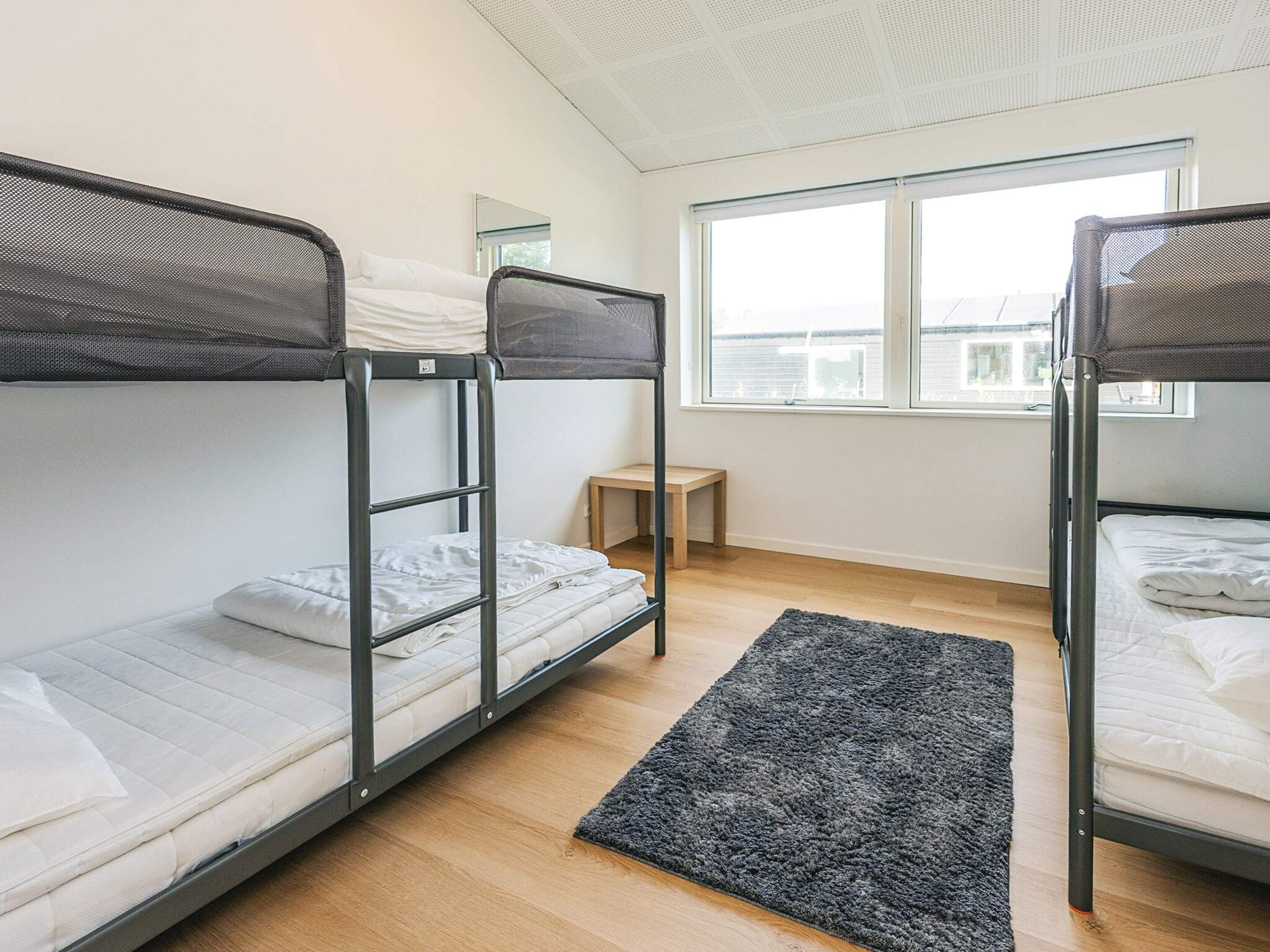 Quarto de dormitório com beliches, um banquinho de madeira e janela com vista.