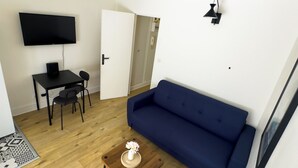 Uma sala de estar com um sofá azul, uma mesa de centro, uma televisão e um espaço de jantar com mesa e cadeiras.