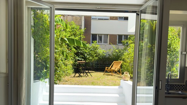 Quarto com porta de vidro deslizante que dá para uma varanda com vista para um jardim e um edifício.