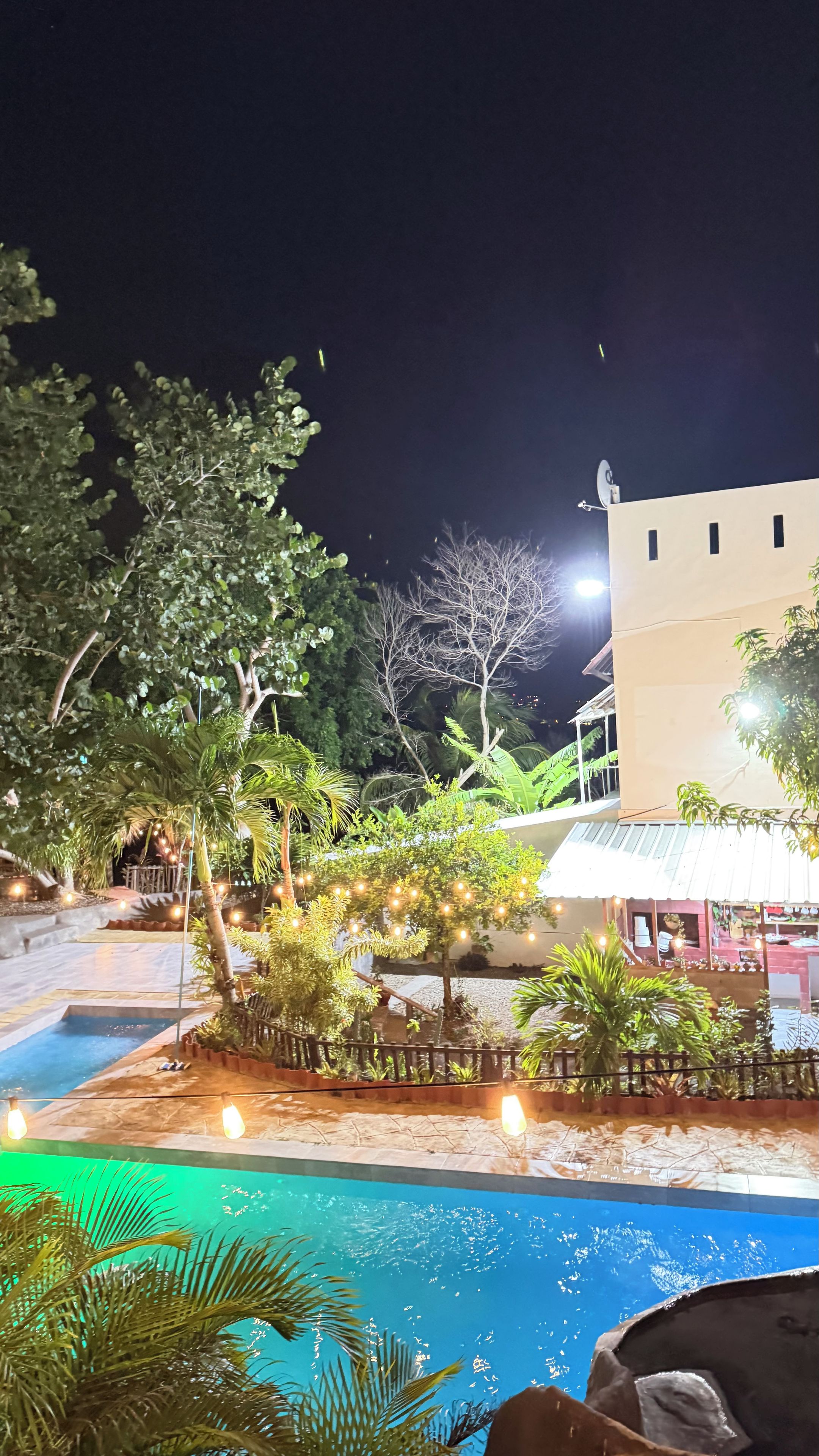 Vista noturna de uma área de piscina com vegetação ao redor e um edifício com antena parabólica.