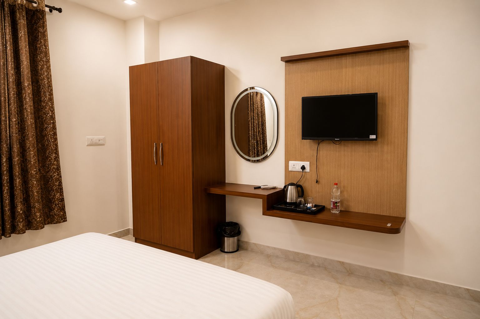 Quarto de hotel com cama, guarda-roupa, televisão e uma pequena prateleira com chaleira, chávena e garrafa.
