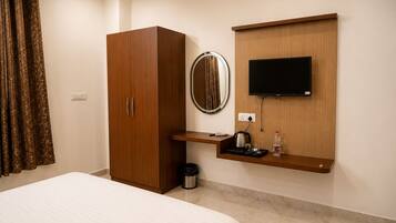 Quarto de hotel com cama, guarda-roupa, televisão e uma pequena prateleira com chaleira, chávena e garrafa.