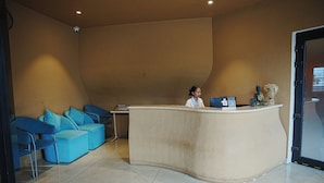 Uma área de recepção com um balcão curvo, um sofá azul e uma pequena mesa com livros.
