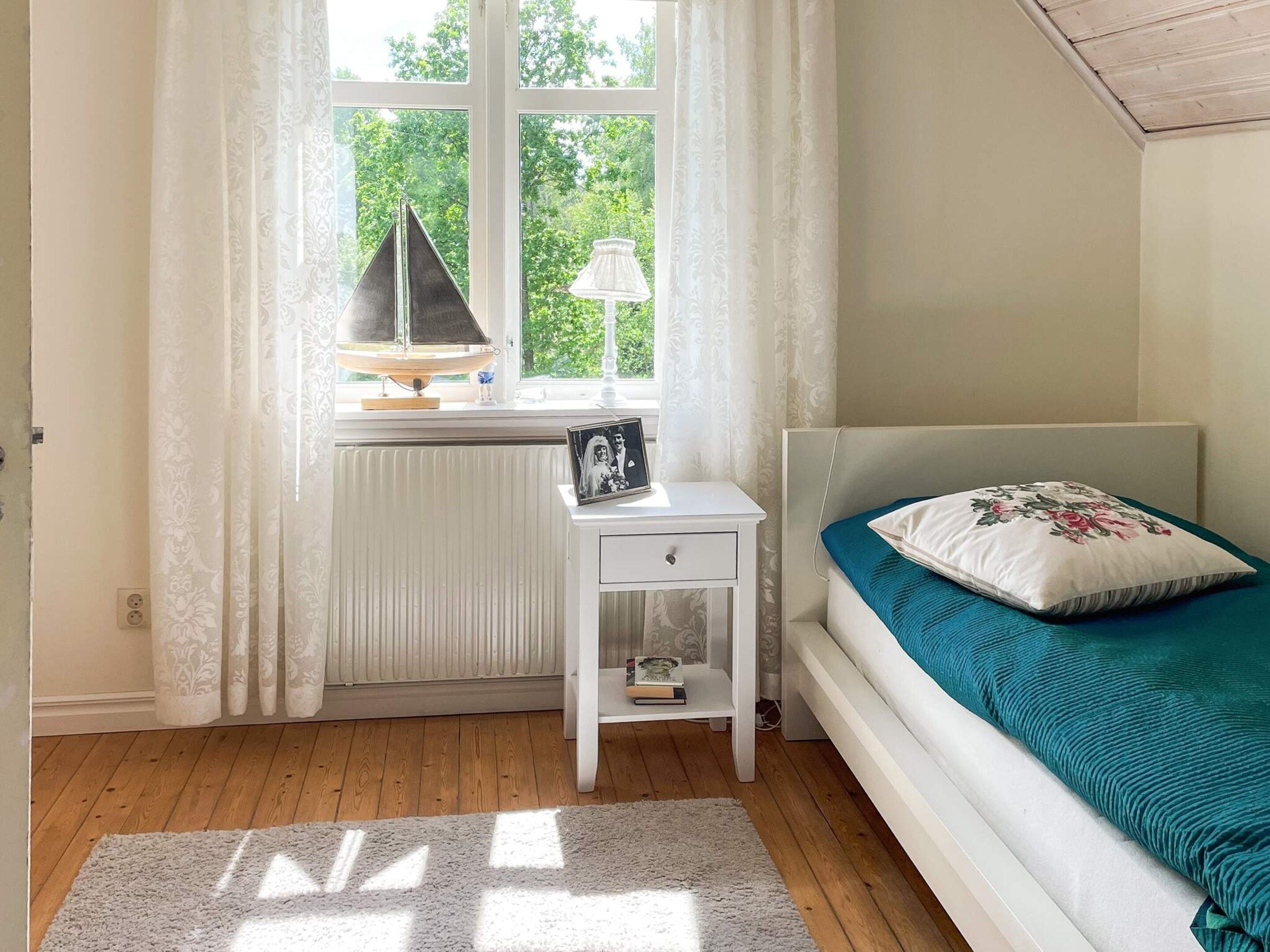 Quarto com cama, mesa de cabeceira, luminária e janela com cortinas.