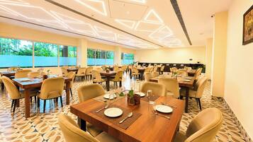 Uma sala de jantar ampla, com várias mesas e cadeiras, grandes janelas e um design geométrico no teto.