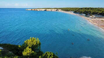 Uma praia costeira com águas azul-claras, areal arenoso e um rochedo ao fundo.