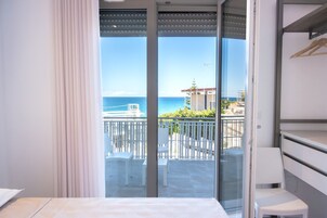 Uma varanda com vista para o mar, cadeiras e mesa brancos.