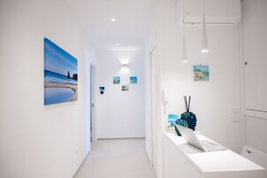 Um corredor com parede branca, um laptop sobre um balcão e uma pintura de uma cena de praia.