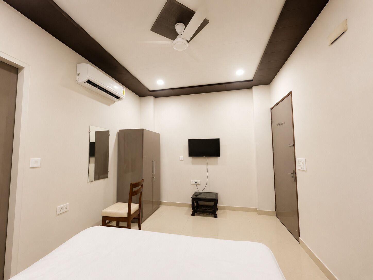 Quarto com cama, cadeira, guarda-roupa, televisão e ar condicionado.