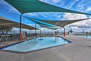 Piscina com áreas sombreadas, espreguiçadeiras e vista do céu.