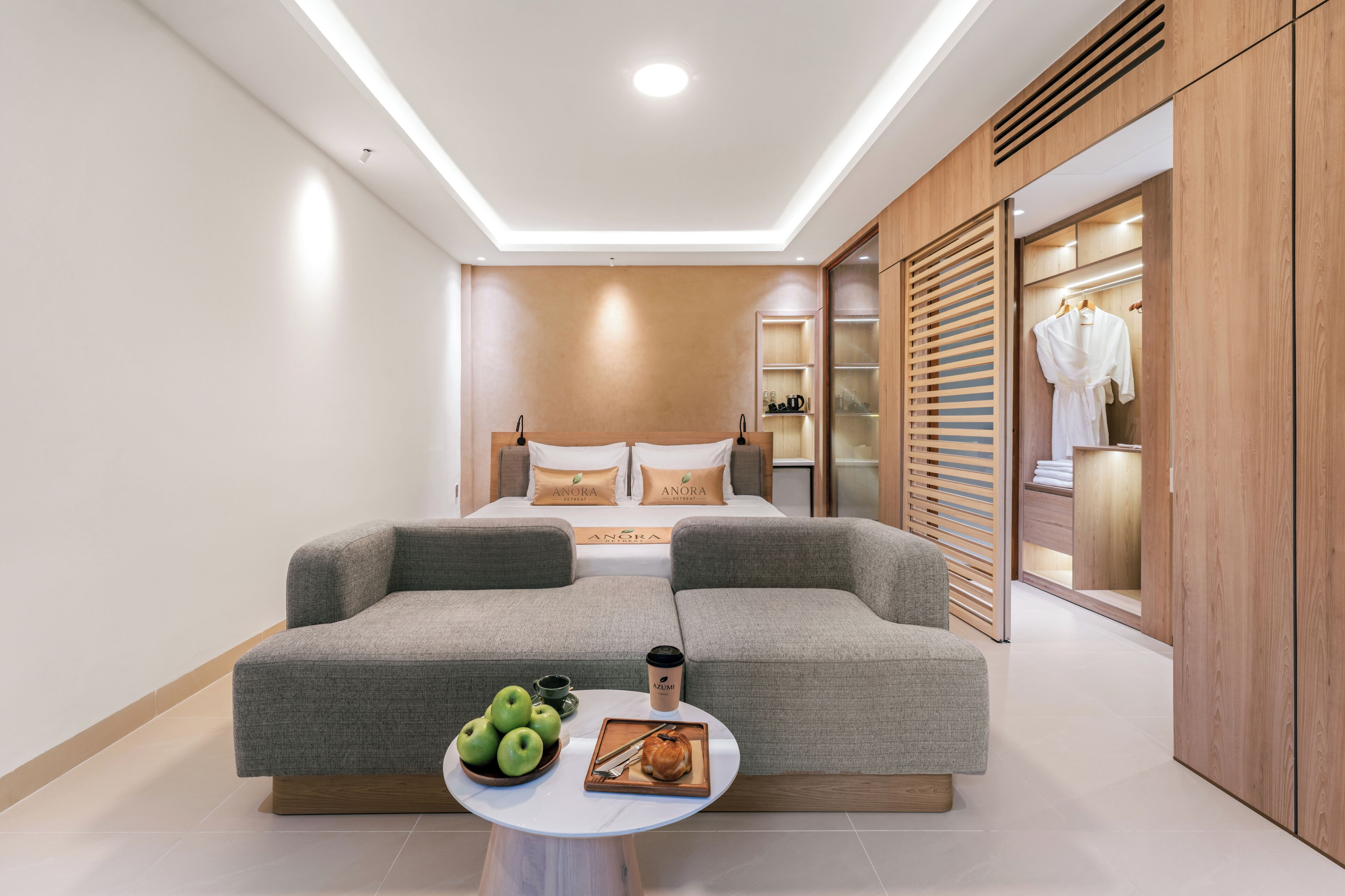 Quarto moderno com sofá-cama, uma mesa de cabeceira com maçãs e uma xícara de café, e um guarda-roupa com um roupão pendurado no interior.