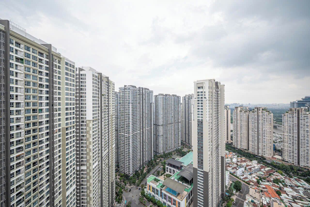 Um complexo de edifícios residenciais altos, com vários prédios de apartamentos, um pátio central e vista para um rio ao longe.