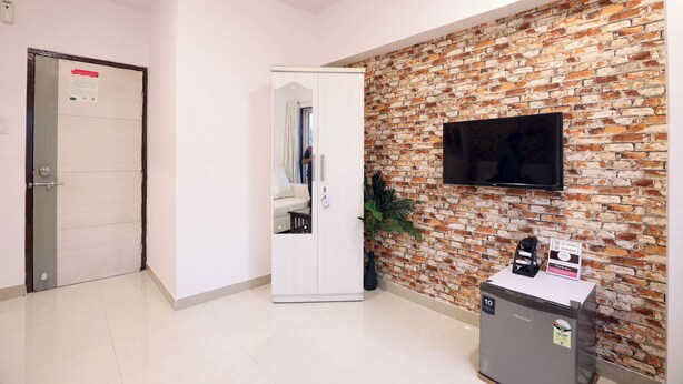 Uma área de recepção com parede de tijolos, uma TV de tela plana, um cabideiro, uma máquina de vendas automática e um guarda-roupa branco.