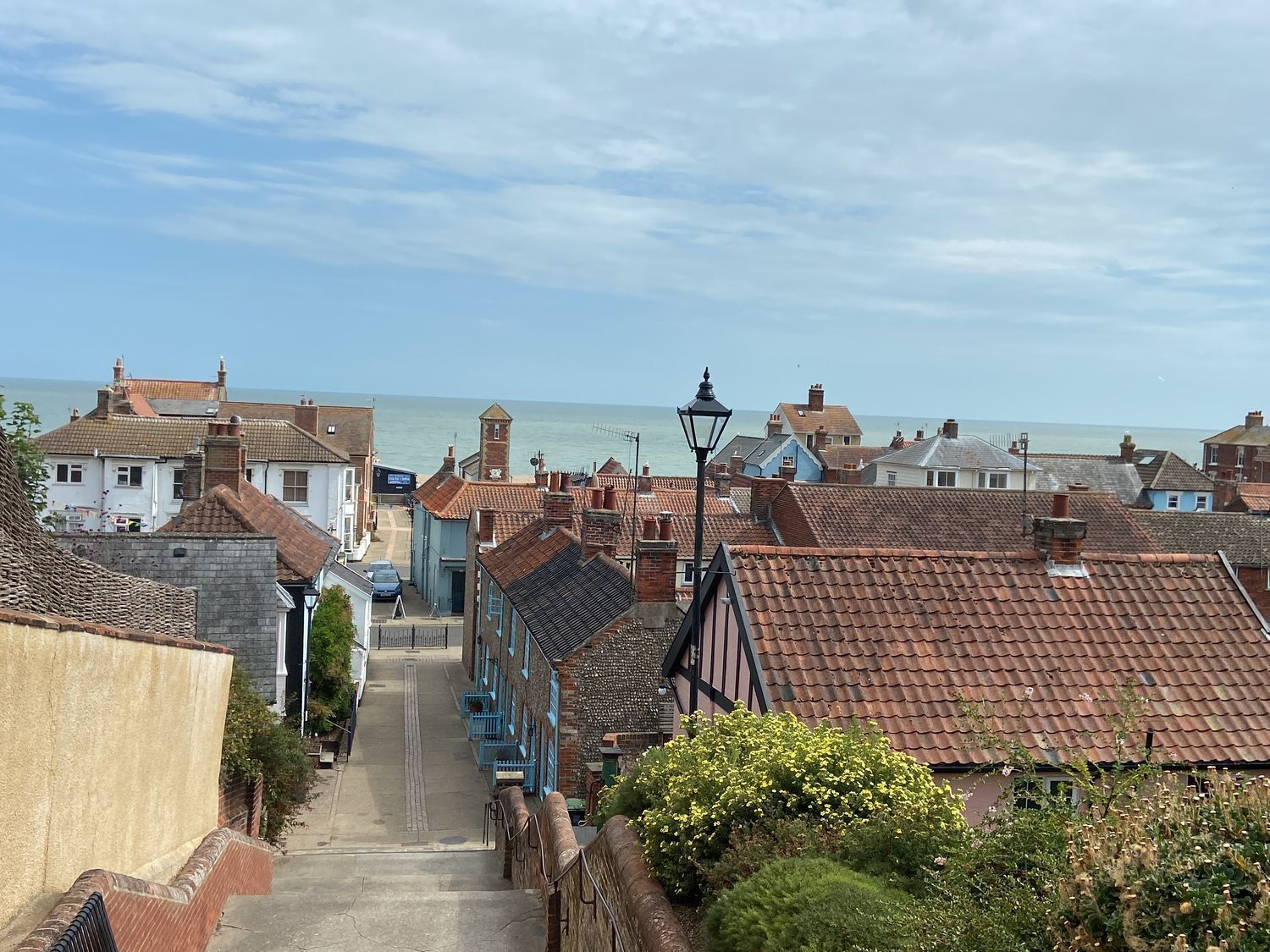 Uma vila costeira com arquitetura tradicional, vista clara do mar e uma rua estreita que leva à orla.