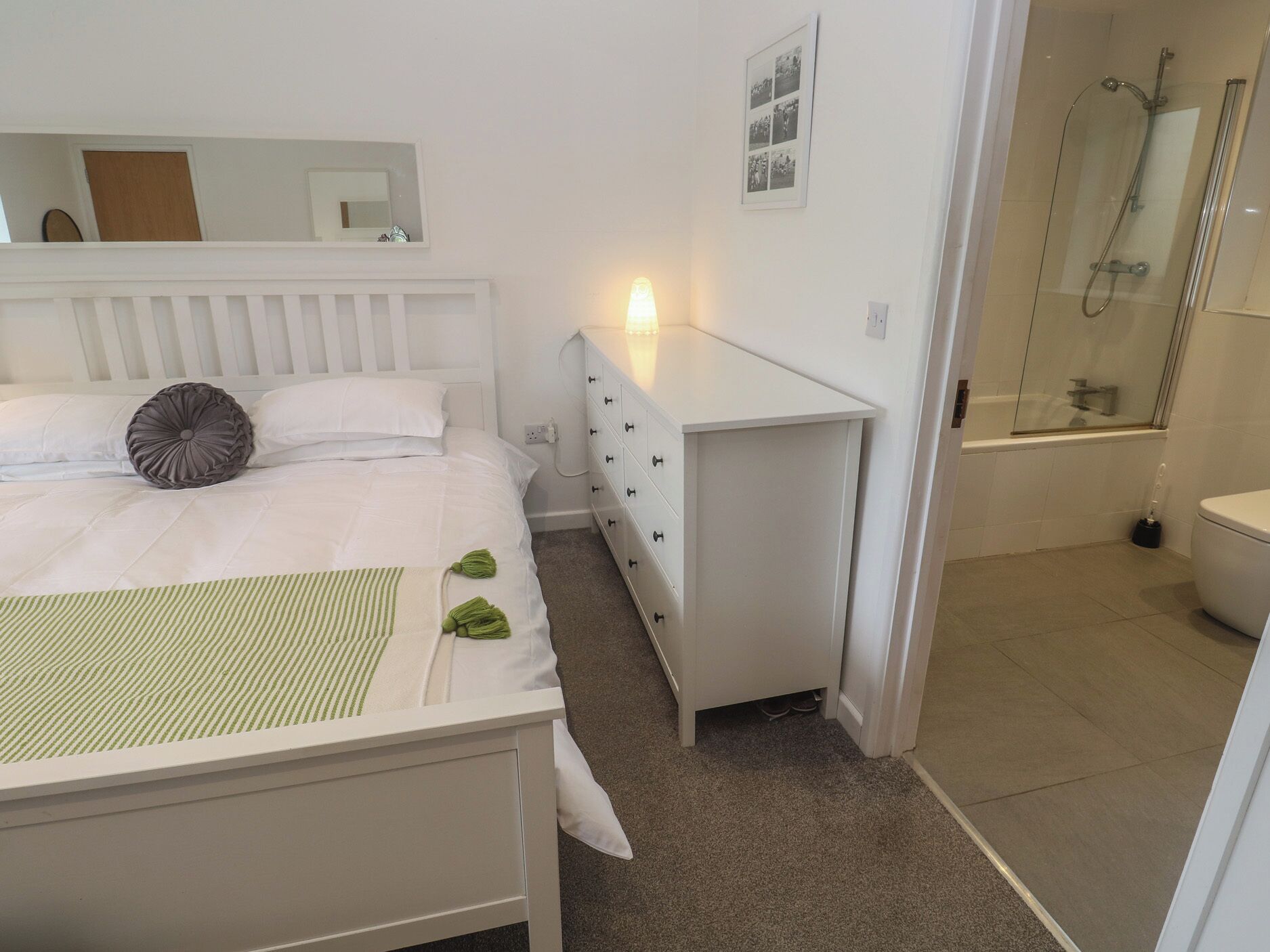 Quarto com cama, mesa de cabeceira, cômoda e banheiro com chuveiro.