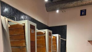 Fileira de cabines de banheiro de madeira, com estrutura metálica e piso de azulejos.