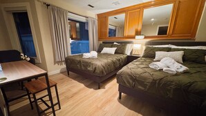 Quarto de hotel com duas camas, uma mesa de madeira e vista para o exterior.