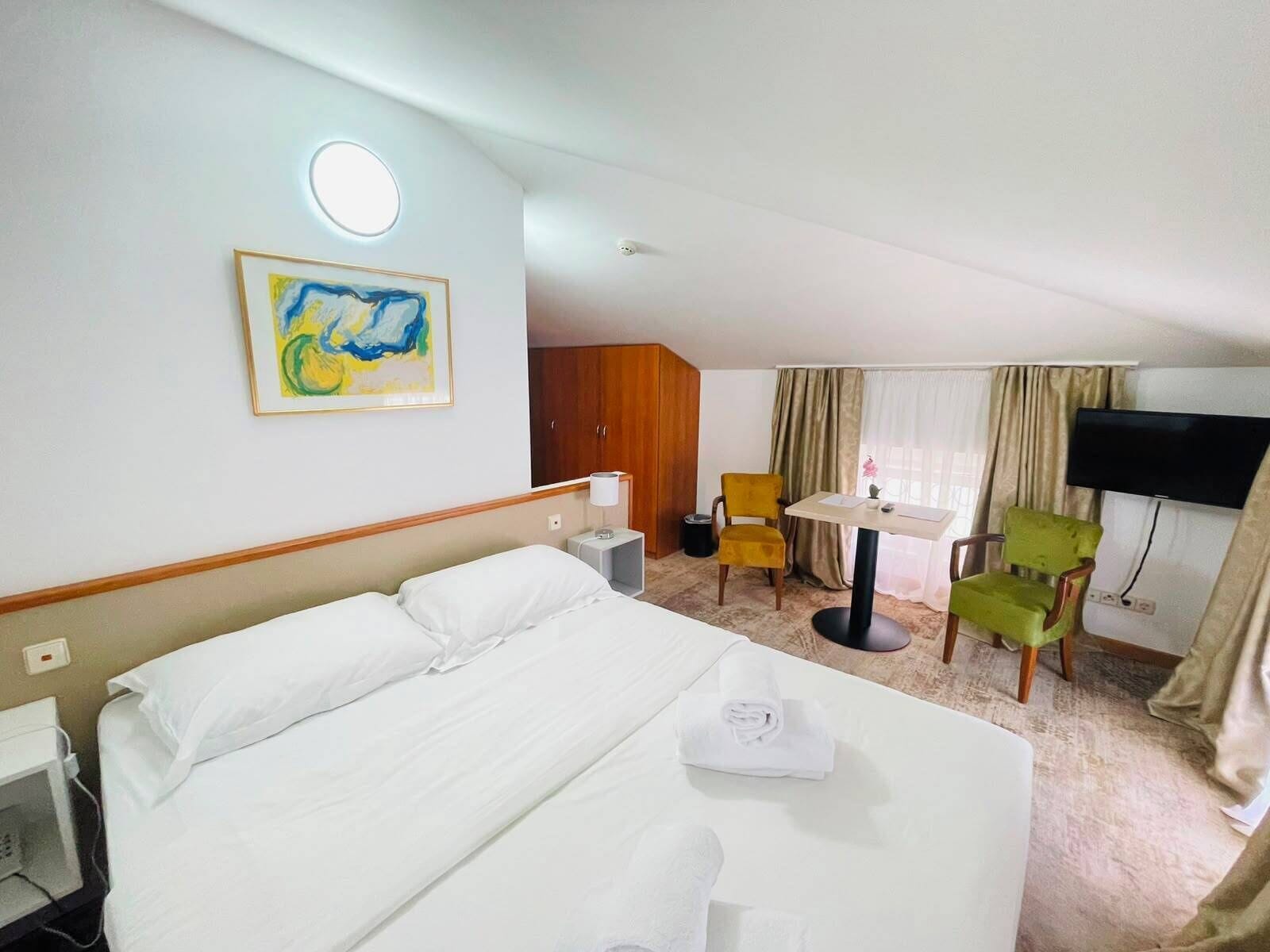Quarto de hotel com cama, escrivaninha, cadeira, televisão e um quadro na parede.