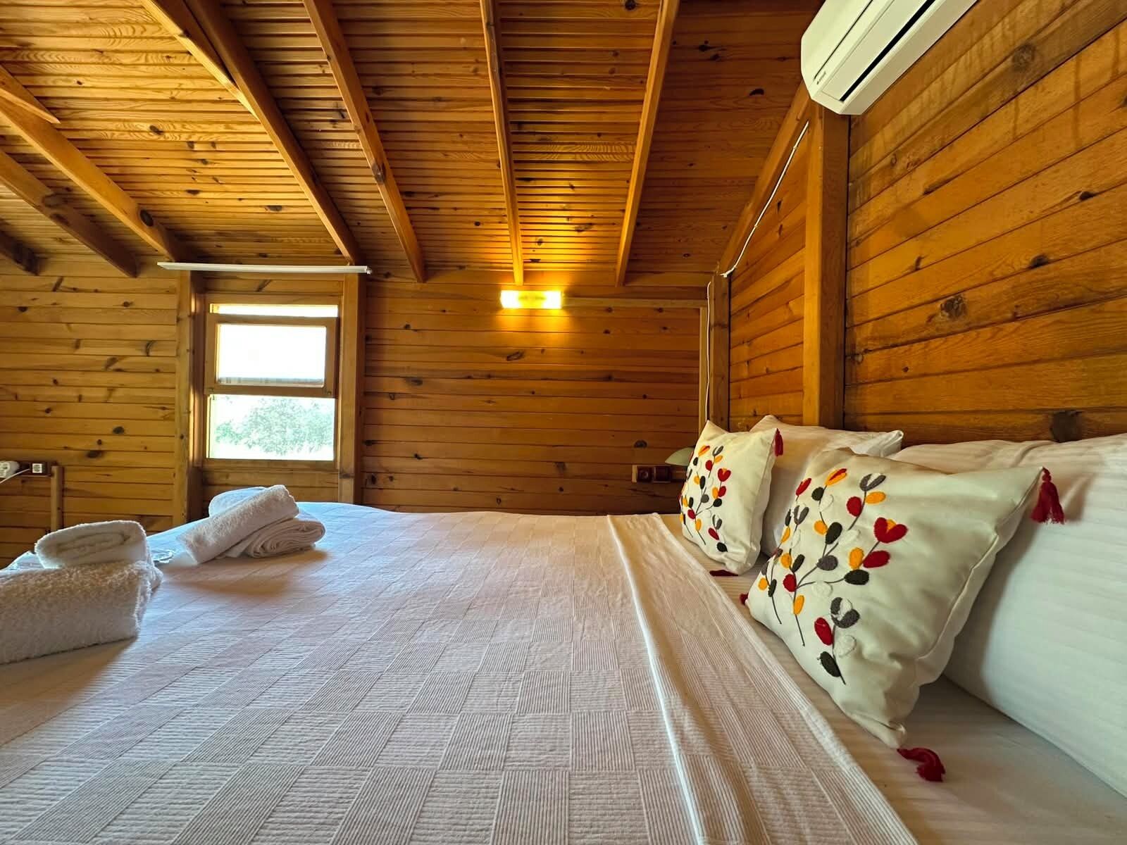 Quarto de cabana de madeira com cama, almofadas, janela e ar condicionado.