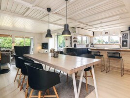 Uma cozinha moderna com mesa de madeira, cadeiras pretas, luminárias pendentes e vista para o exterior.