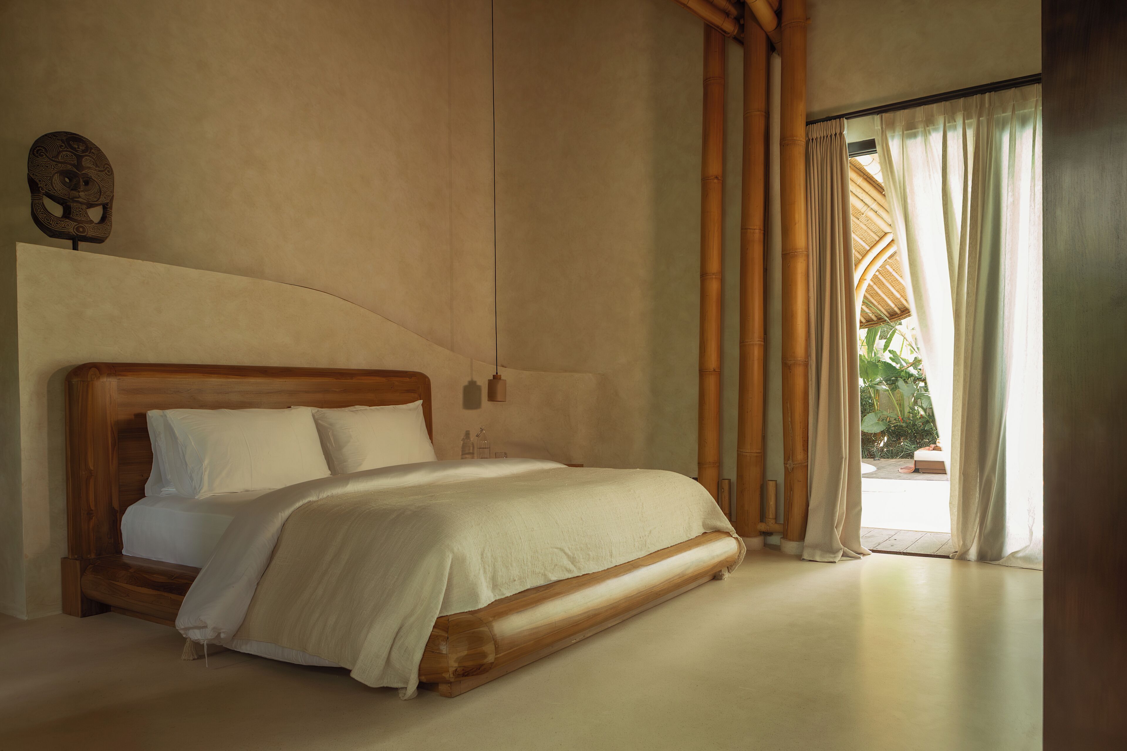 Quarto com cama de madeira, cabeceira e vista para o exterior através de uma janela com cortinas.