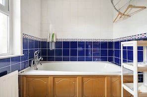 Casa de banho com banheira branca, armários de madeira e paredes com azulejos azuis.