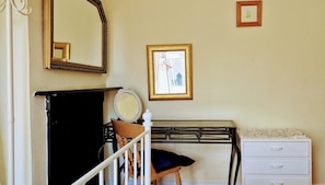 Um quarto com lareira, espelho, cama, cômoda e um quadro na parede.