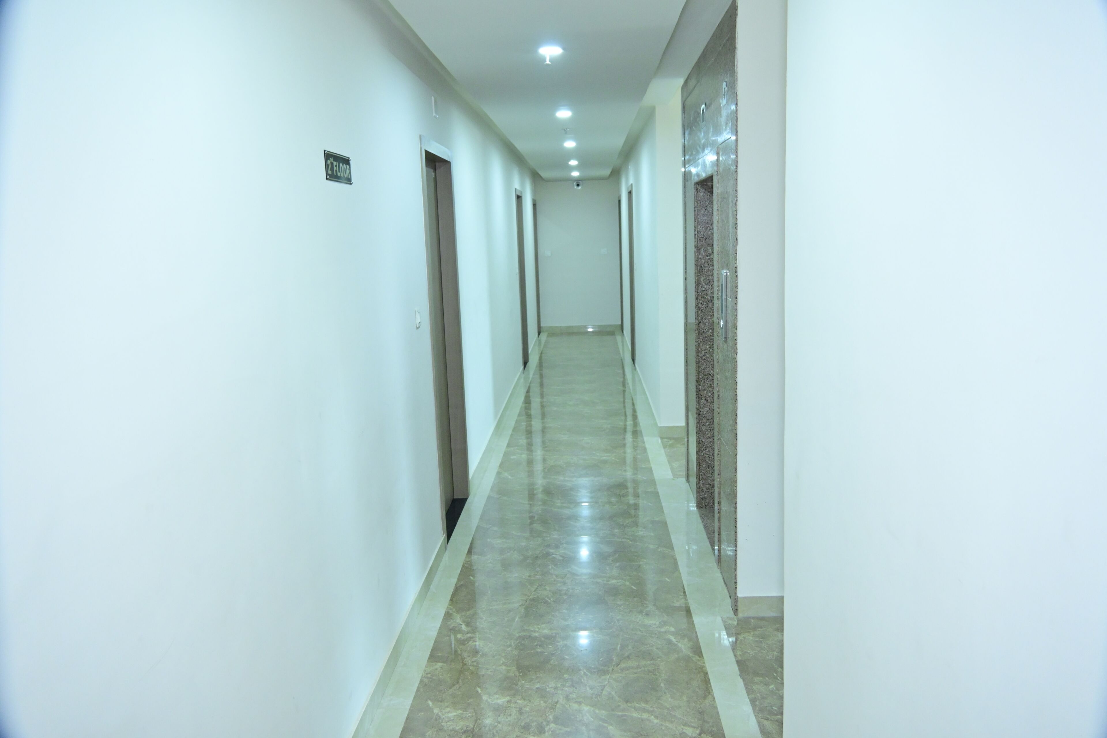 Um corredor comprido e estreito com piso de mármore e paredes brancas.