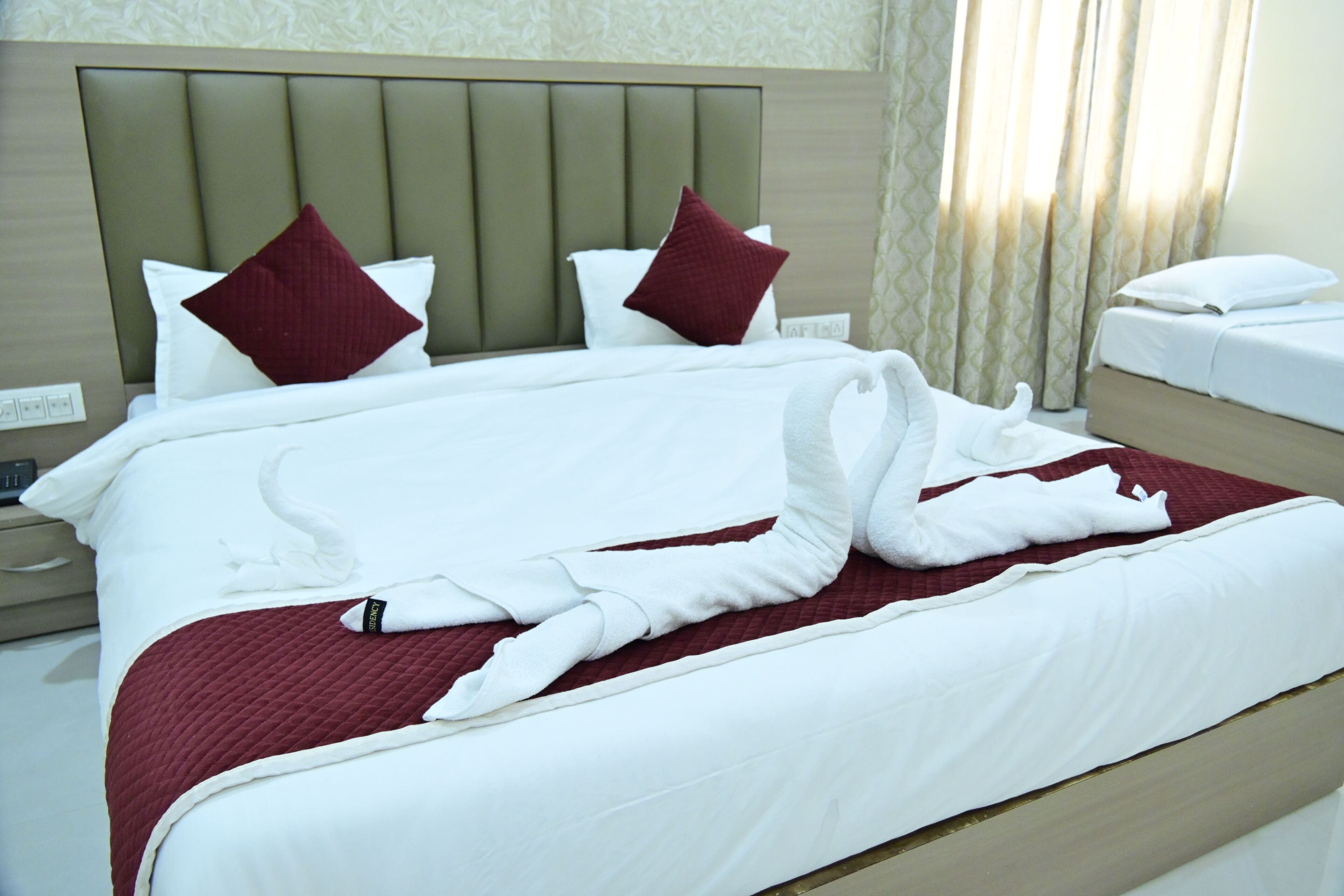 Quarto de hotel com uma cama grande, duas almofadas, uma mesa de cabeceira e uma janela com cortinas.