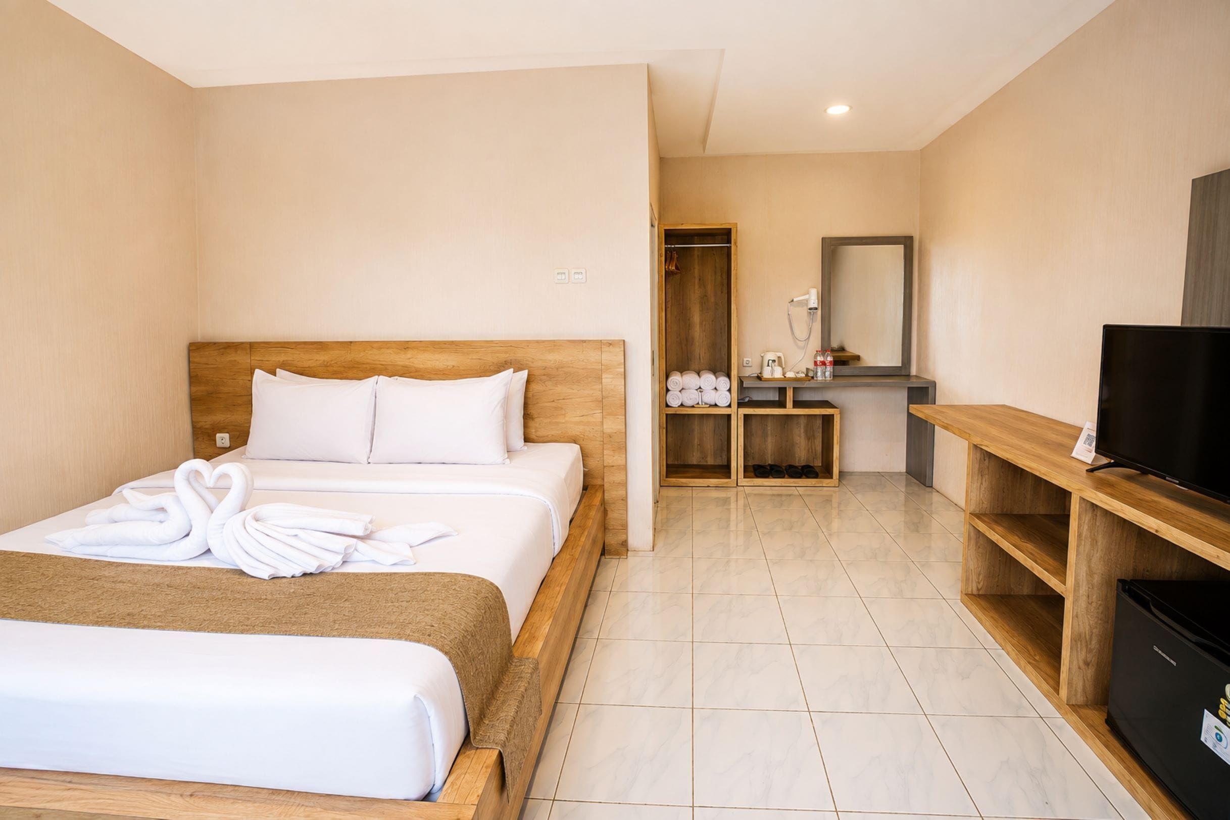 Quarto de hotel com cama, televisão, secretária com espelho e zona de duche.