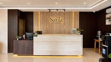 Uma receção com acabamento em madeira, um ecrã digital e uma placa a indicar 'Savia Hotel & Resort'.