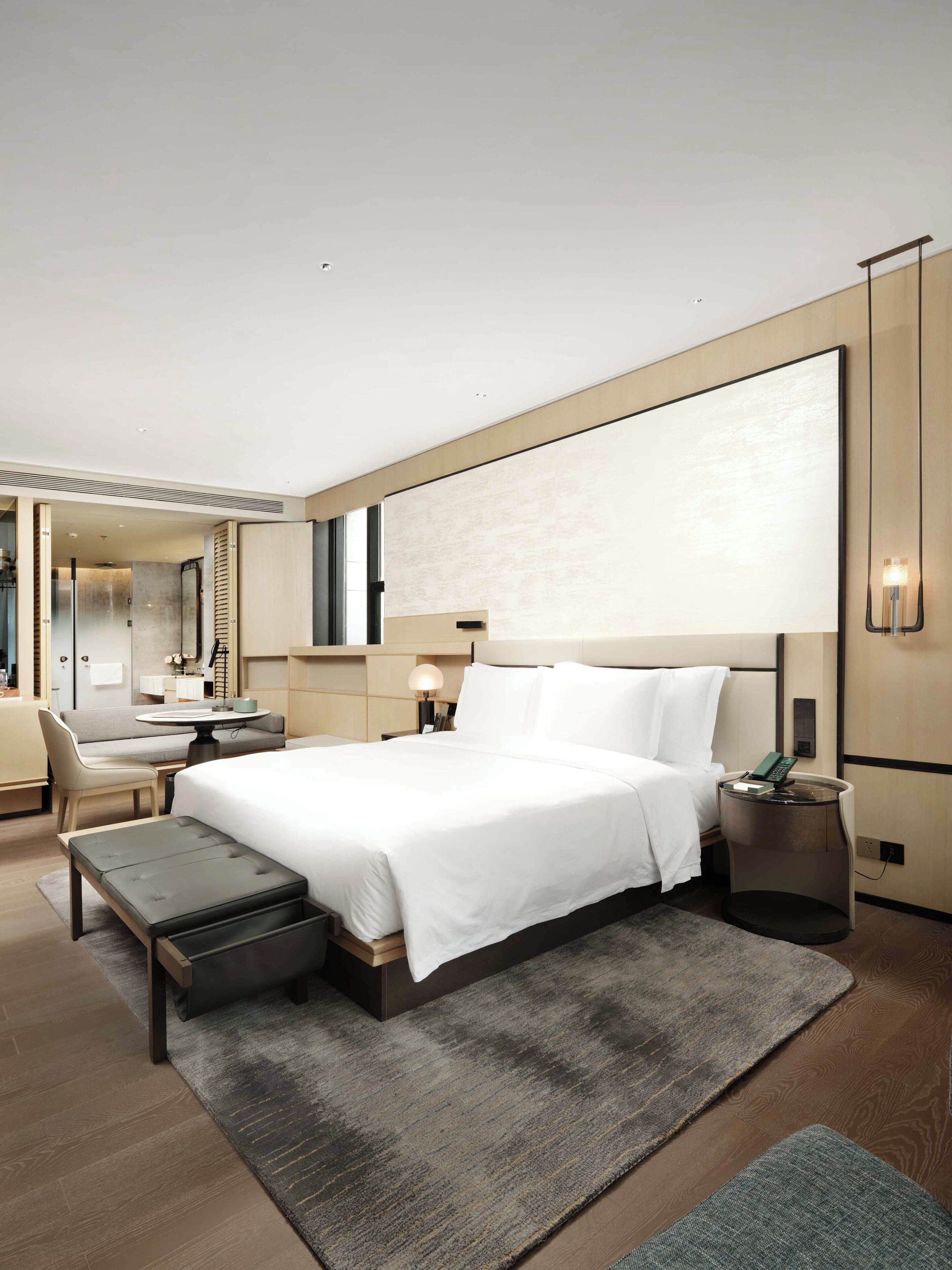 Quarto de hotel moderno com uma cama grande, mesas de cabeceira, escrivaninha e uma cadeira.