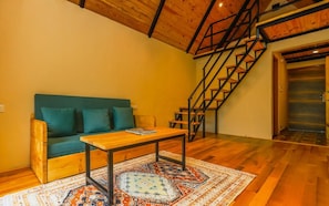 Uma sala de estar acolhedora com teto de madeira, um sofá com almofadas azuis e uma mesa de centro, além de um tapete estampado.