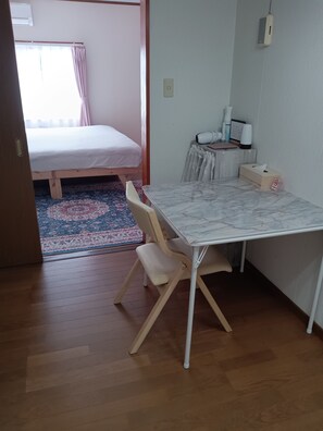 Um quarto com uma cama, uma mesa com cadeiras, uma pequena escrivaninha com uma luminária e um radiador.