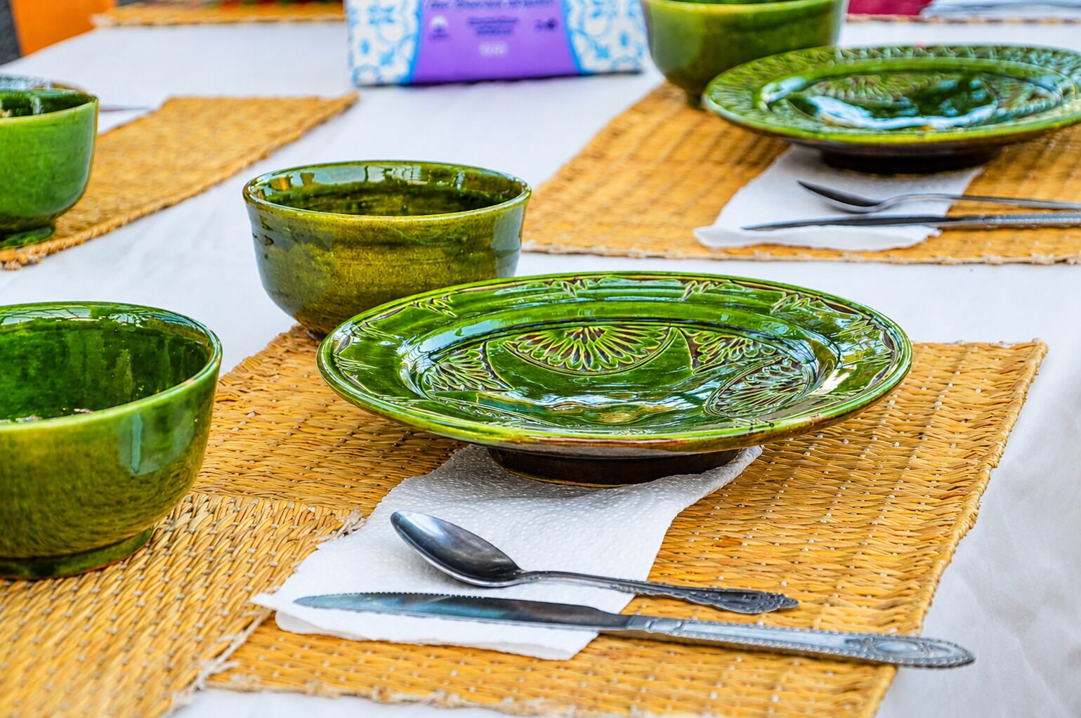 Mesa posta com tigelas de cerâmica verde, uma colher e uma faca sobre um jogo americano tecido.