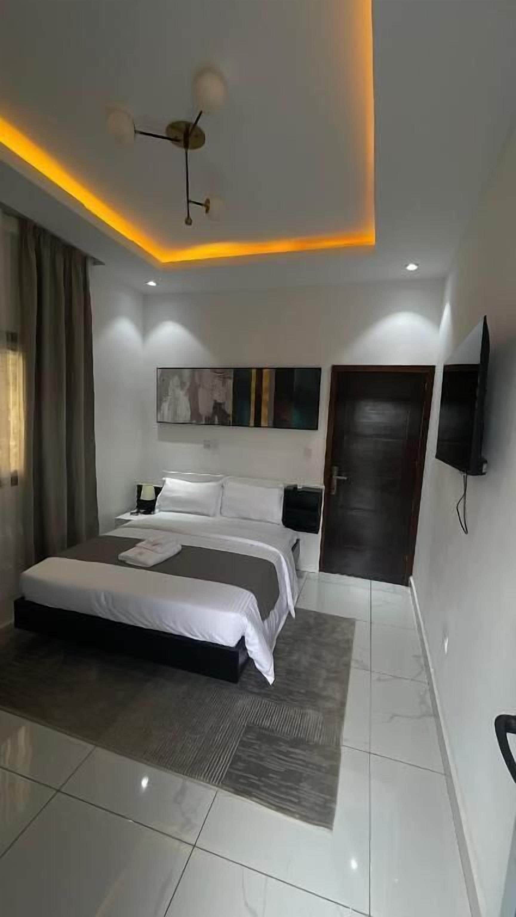 Quarto moderno com uma cama grande, mesas de cabeceira, uma luminária no teto, uma TV de tela plana e uma porta.